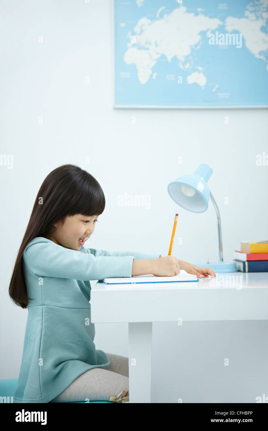 A girl writing on a book in front of the desk Stock Photo - Alamy