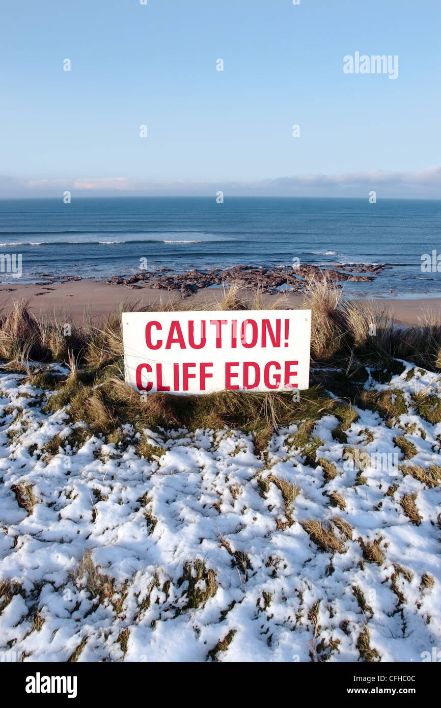 a red caution sign on a cliff edge in snow covered ballybunion Stock ...