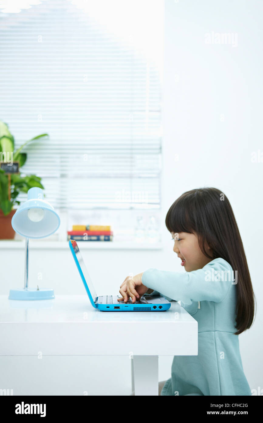 A smiling girl pushing the keyboard of a laptop in front of the desk ...