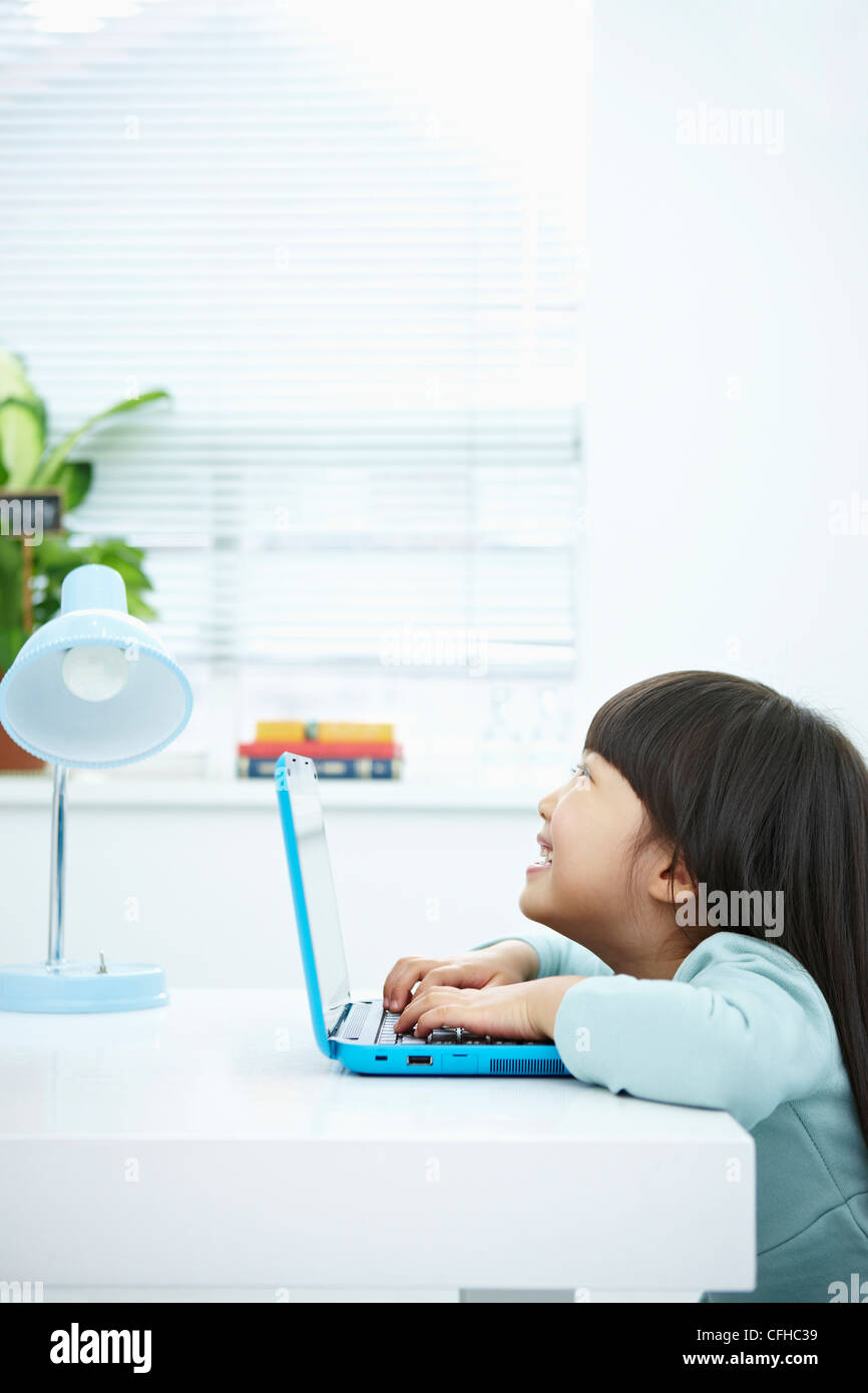 A smiling girl pushing the keyboard of a laptop in front of the desk ...