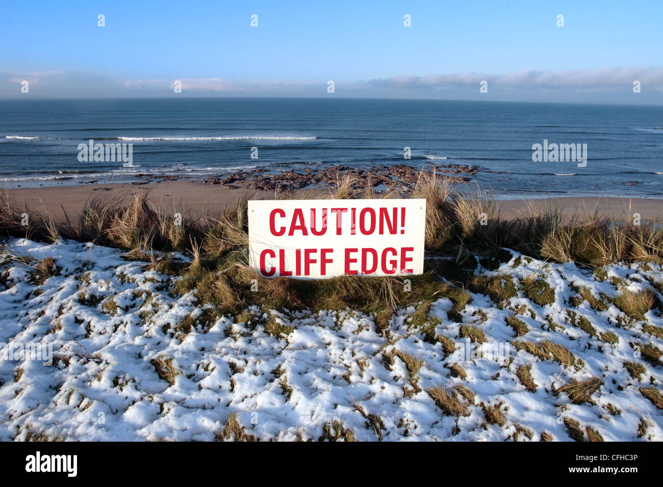 a red caution sign on a cliff edge in snow covered ballybunion Stock ...