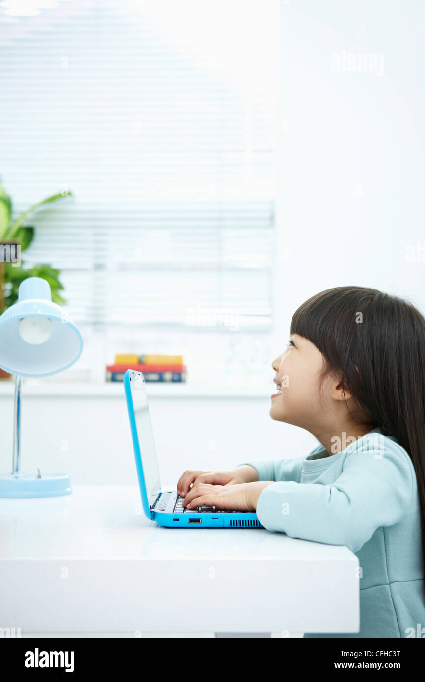 A smiling girl pushing the keyboard of a laptop in front of the desk ...