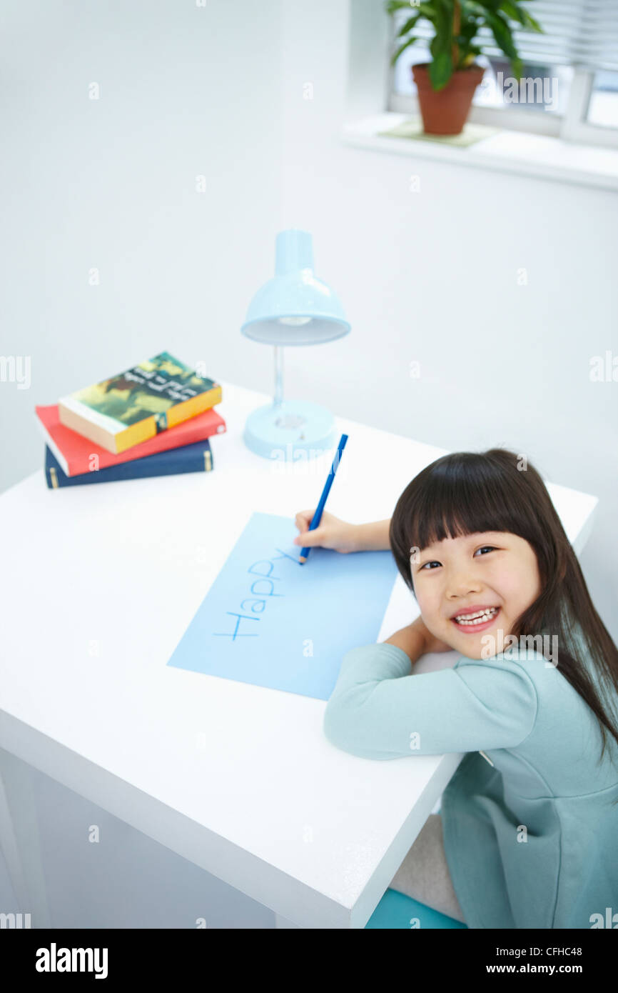 A smiling girl writing 'Happy' on the blue paper with a blue colored ...