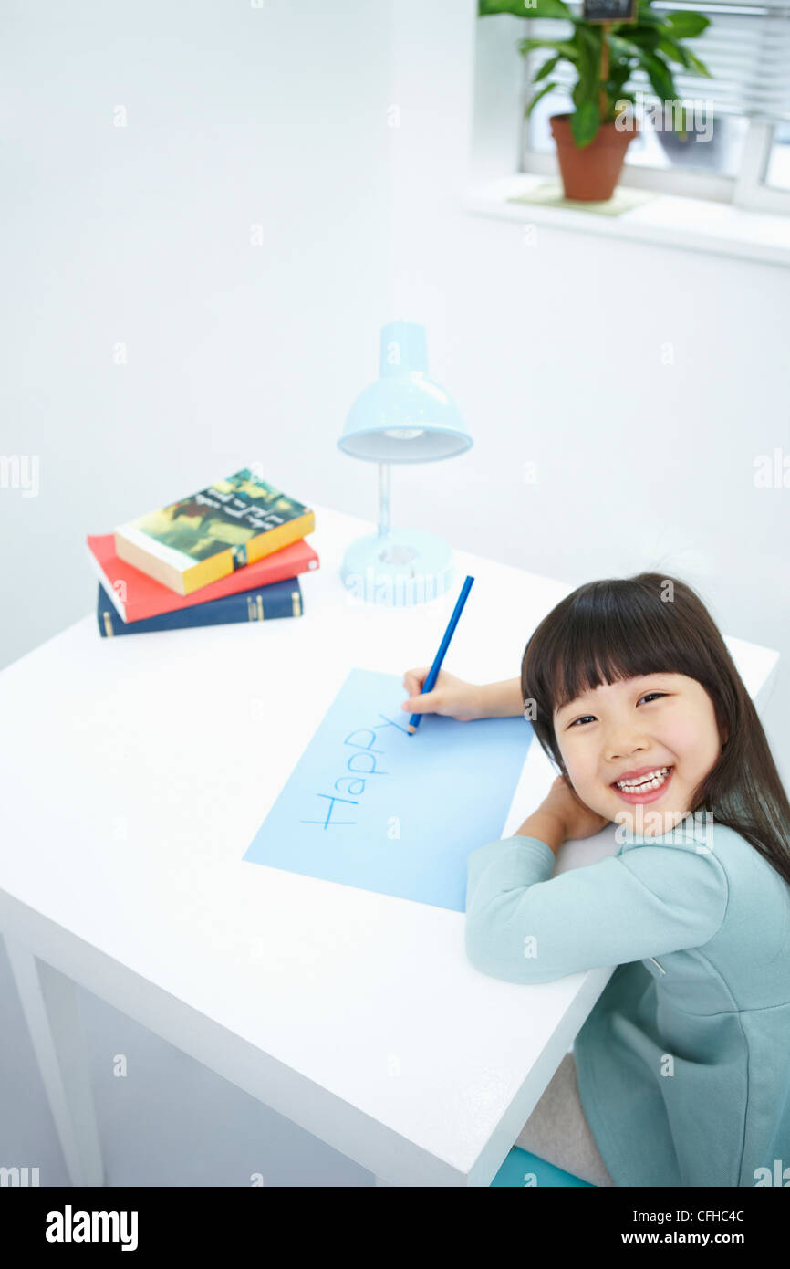 A smiling girl writing 'Happy' on the blue paper with a blue colored ...