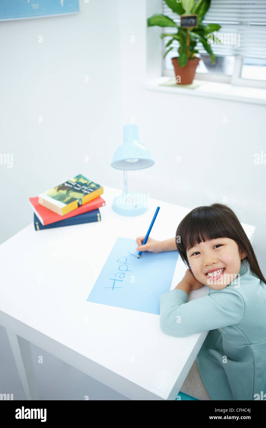 A smiling girl writing 'Happy' on the blue paper with a blue colored ...