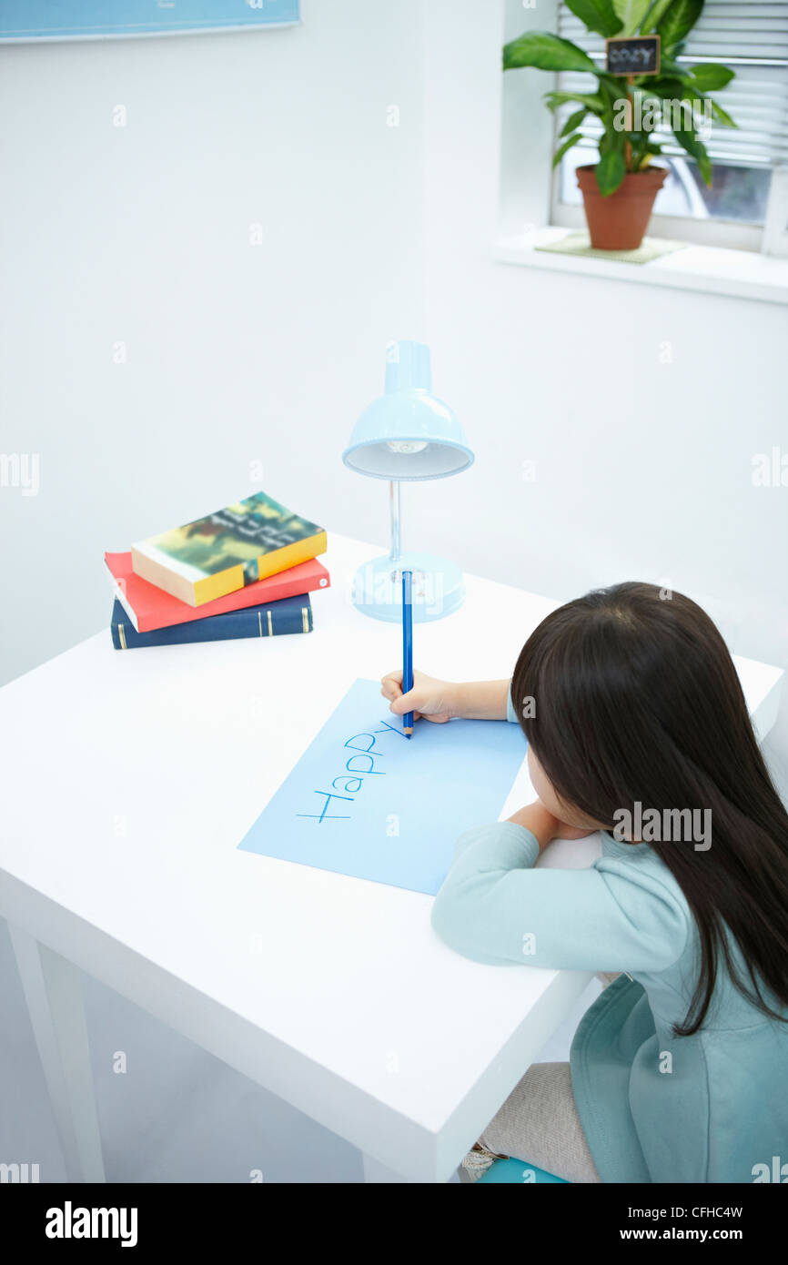 A girl writing 'Happy' on the blue paper with a blue colored pencil ...