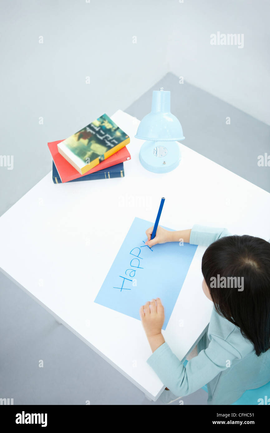 A girl writing 'Happy' on the blue paper with a blue colored pencil ...