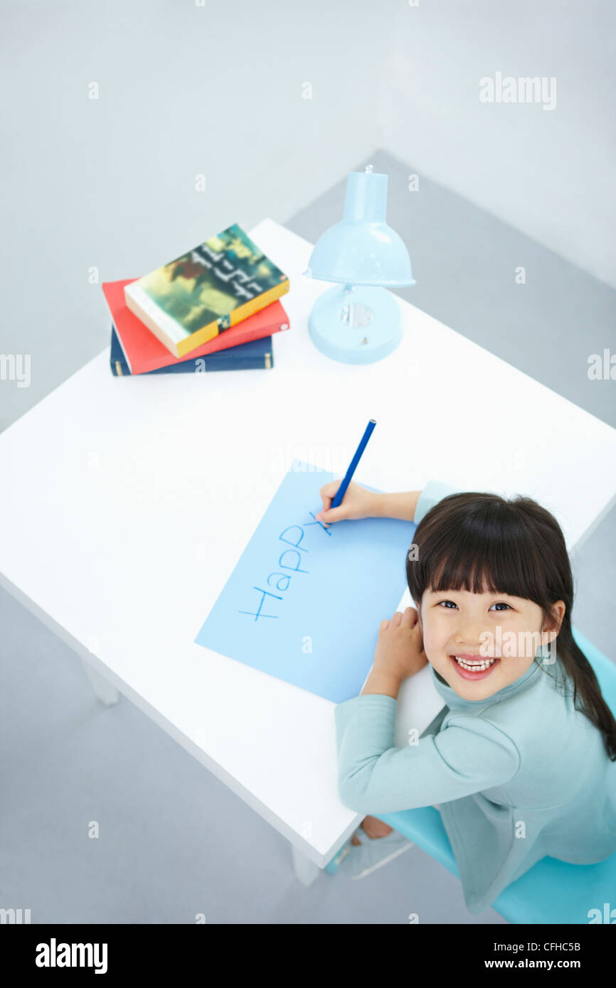 A smiling girl writing 'Happy' on the blue paper with a blue colored ...
