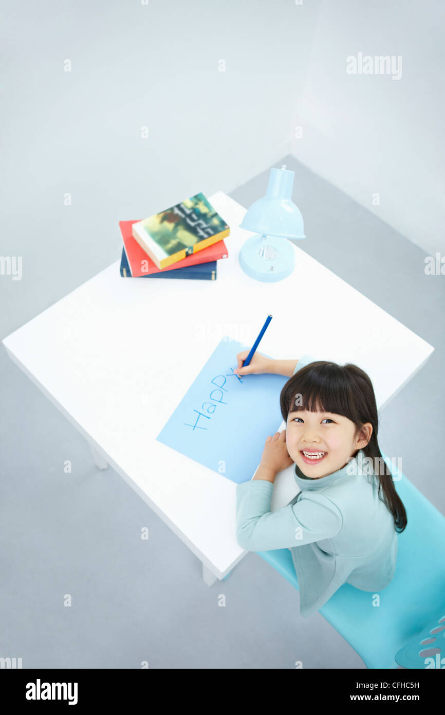 A smiling girl writing 'Happy' on the blue paper with a blue colored ...