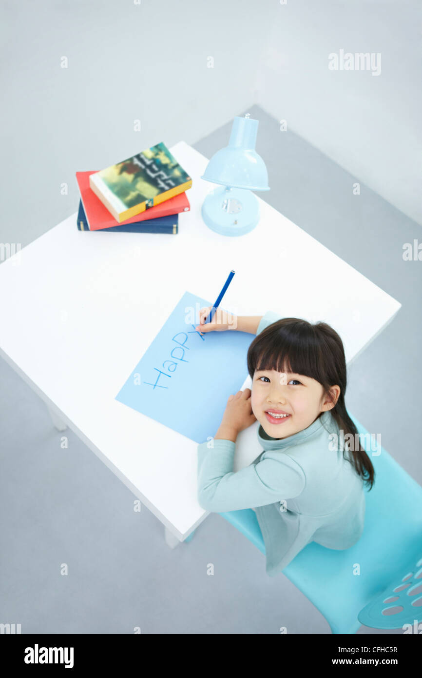 A smiling girl writing 'Happy' on the blue paper with a blue colored ...