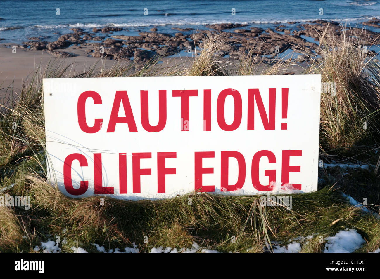 a red caution sign on a cliff edge in snow covered ballybunion Stock ...