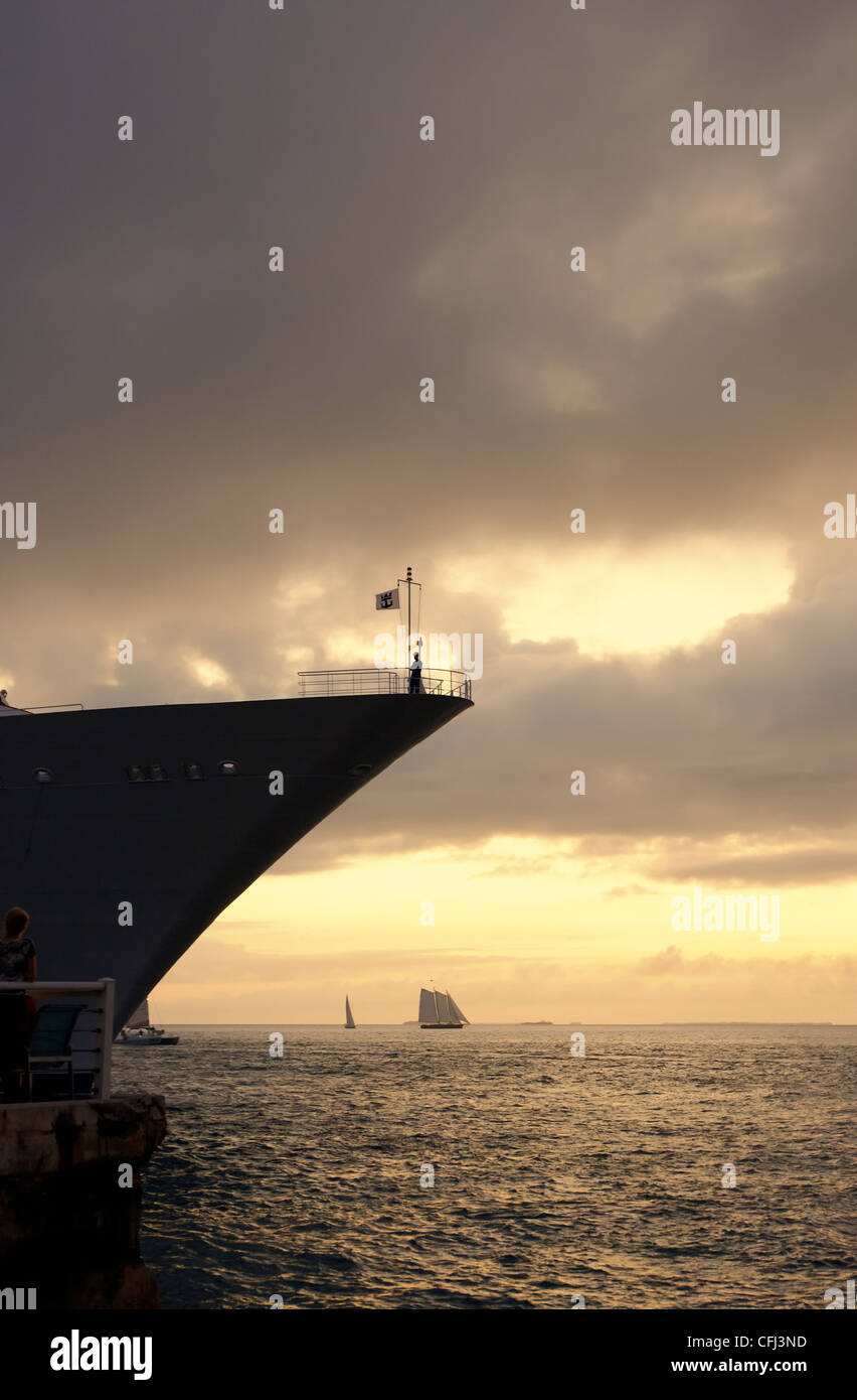 An anonymous person standing on the front of a ship with sunset sky ...