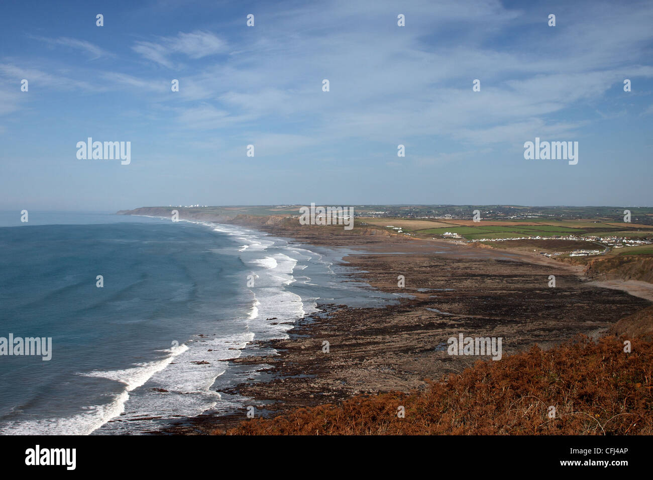 A rugged beach in Cornwall with fields and villages in the background ...