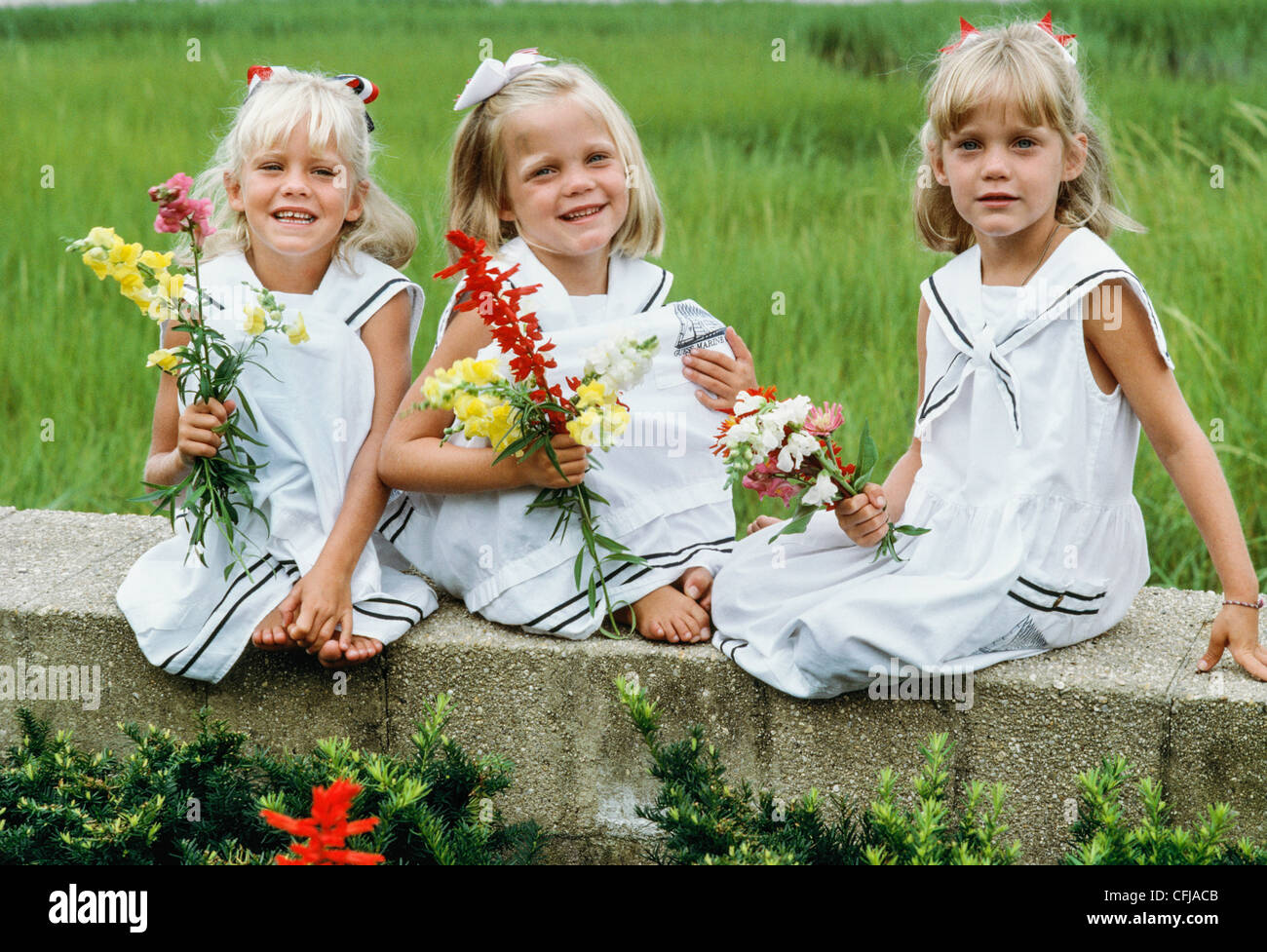 Cute blonde triplet sisters sitting on a garden wall. Series one of ...