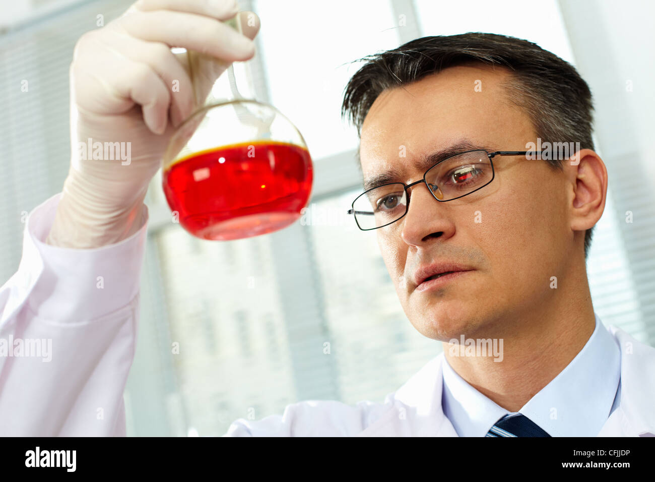 Serious clinician looking at flask with red liquid in laboratory Stock ...