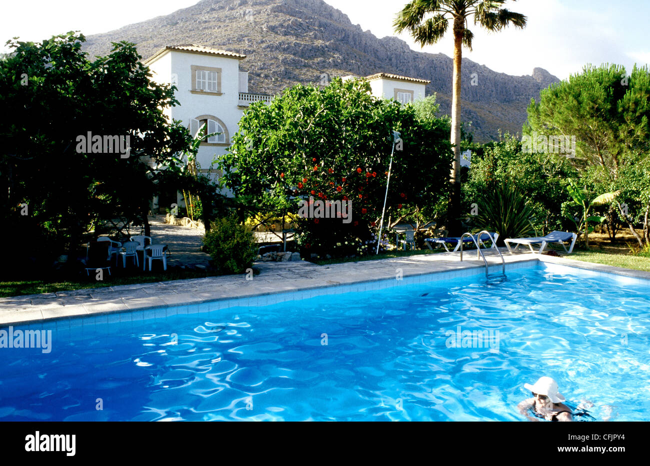 A figure in a hat swims in a blue swimming pool Majorca Spain Stock ...