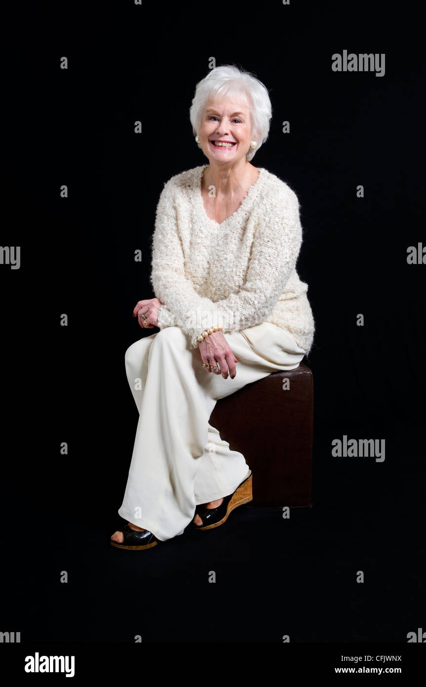 Full length shot of attractive senior lady sat down taken against a ...