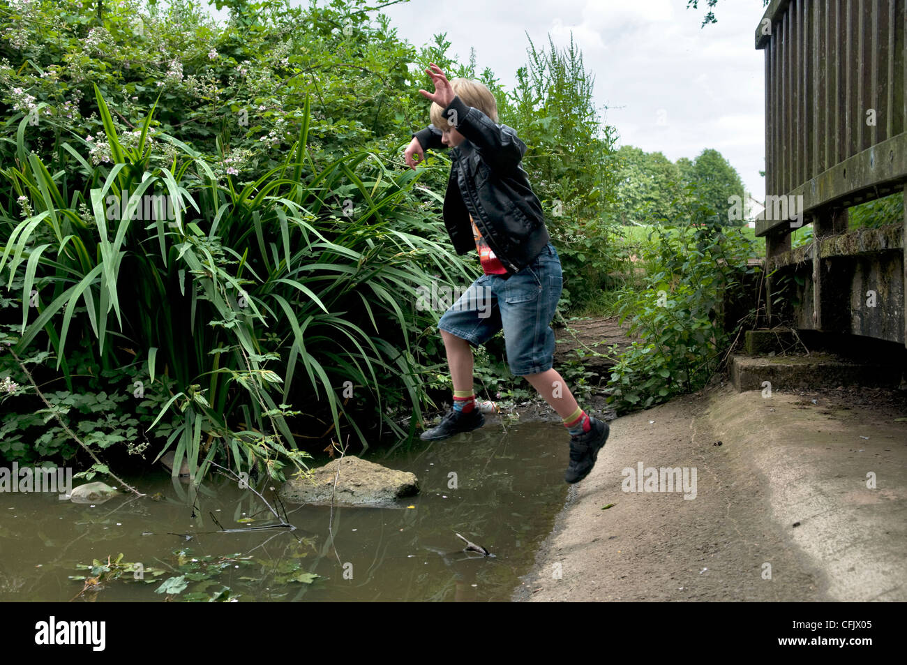 8 year old Caucasian boy jumping onto rock over stream at Barrs Court ...