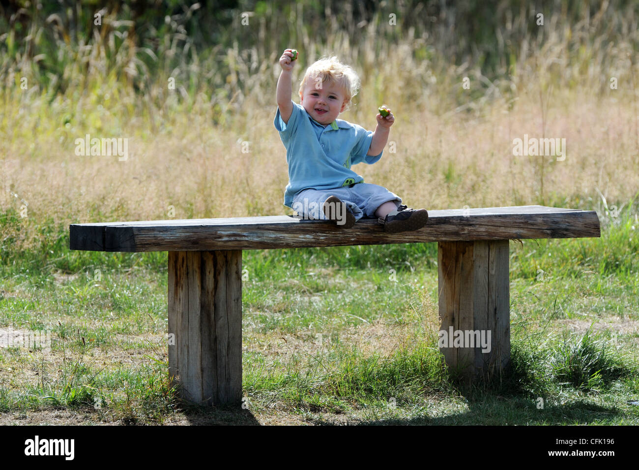 Baby boy sitting on wooden bench uk Stock Photo - Alamy