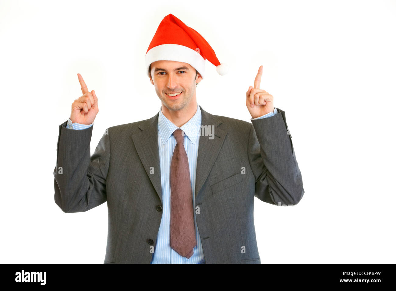 Smiling young businessman in Santa hat pointing finger up at copy space ...