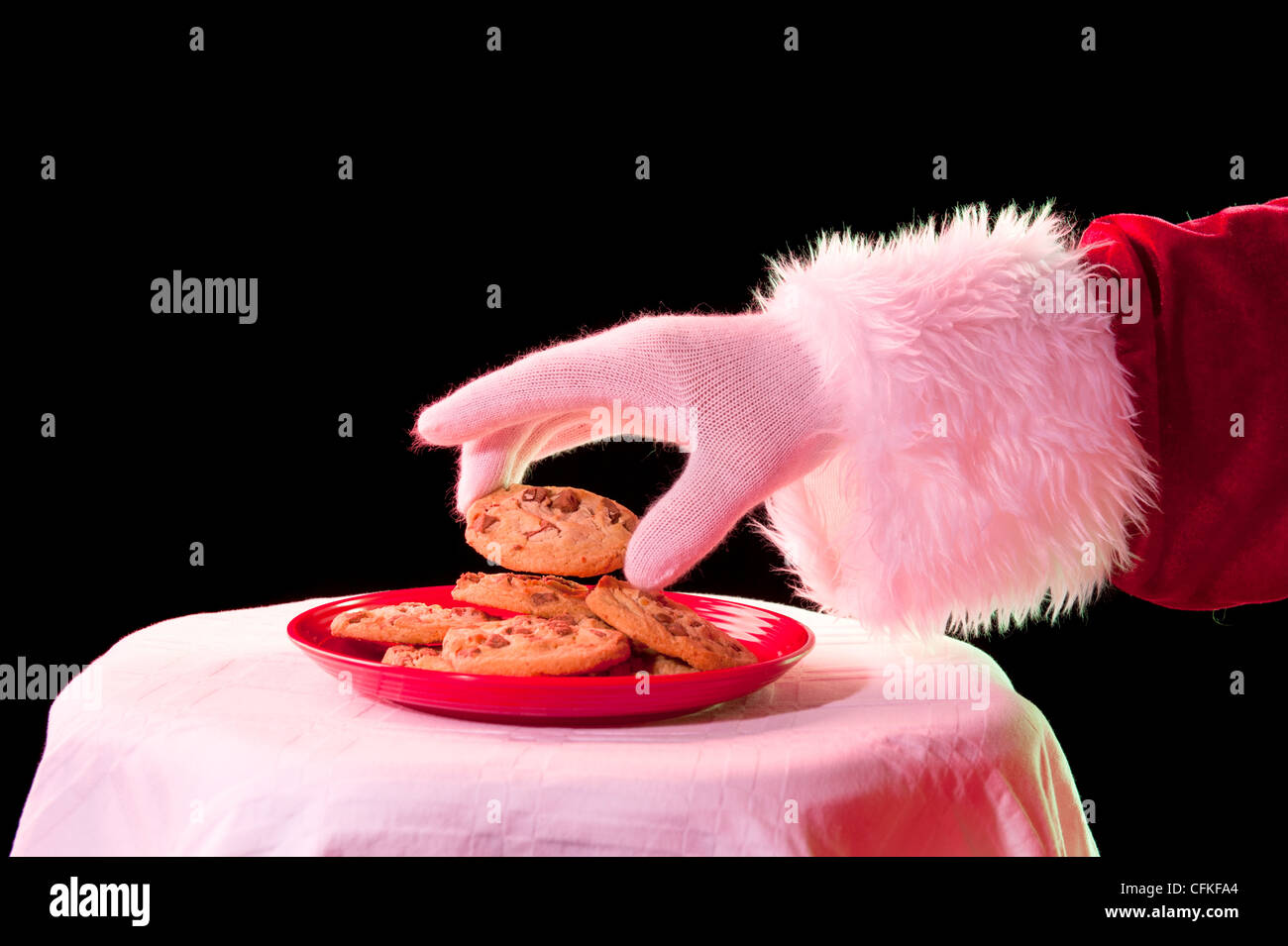 Santa Claus reaching for a fresh chocolate chip cookie from a red plate ...