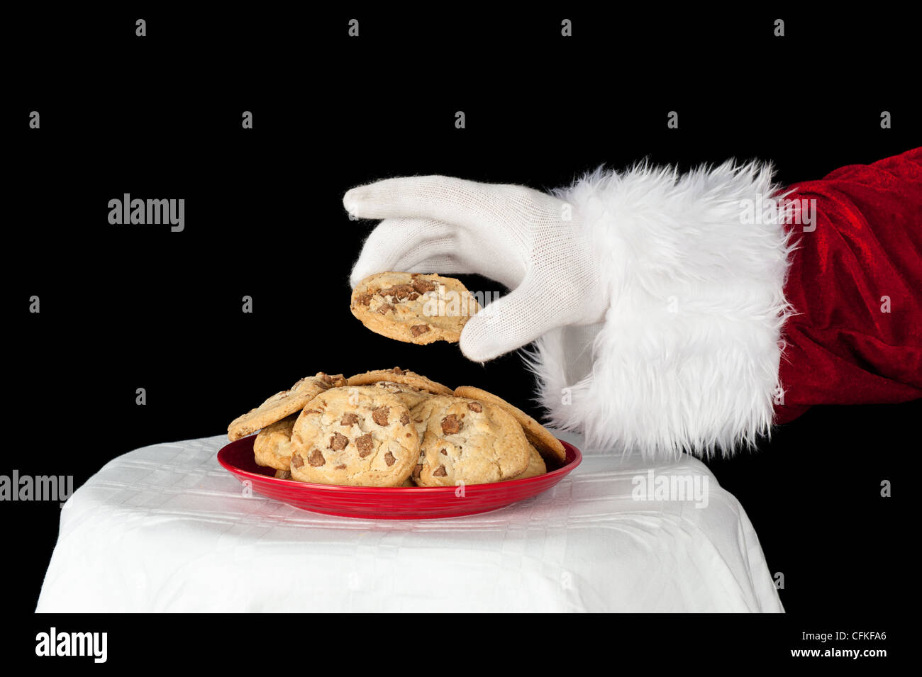 Santa Claus reaching for a fresh chocolate chip cookie from a red plate ...