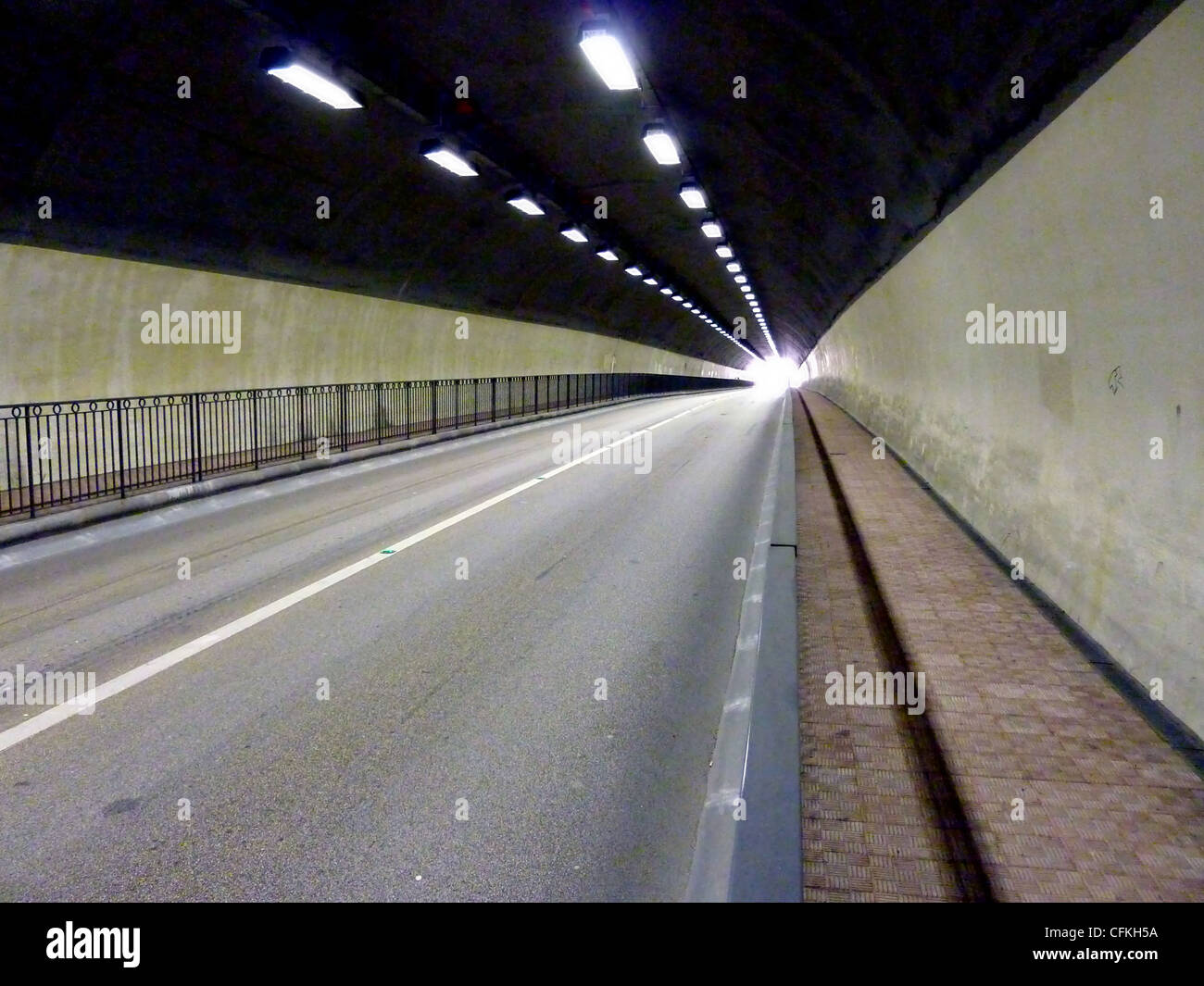 Inside a tunnel with a sidewalk, white walls, black roof and fence ...