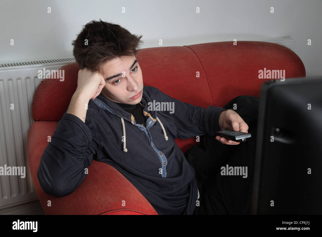 Young man watching TV, holding the remote control, looking bored Stock ...