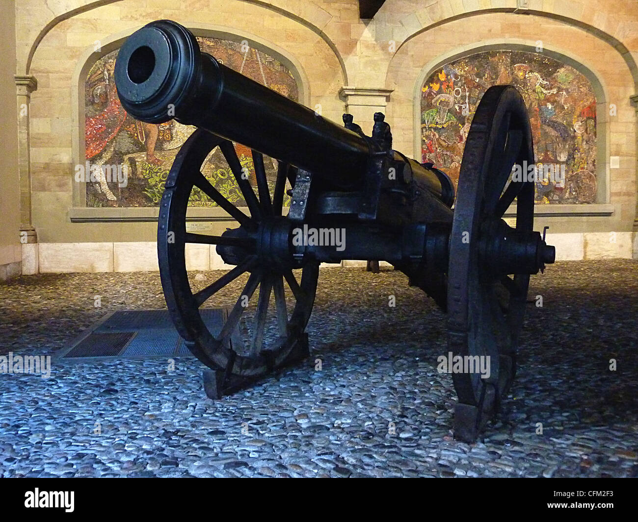 Black cannon supported by two wheels with paintings behind in the od ...