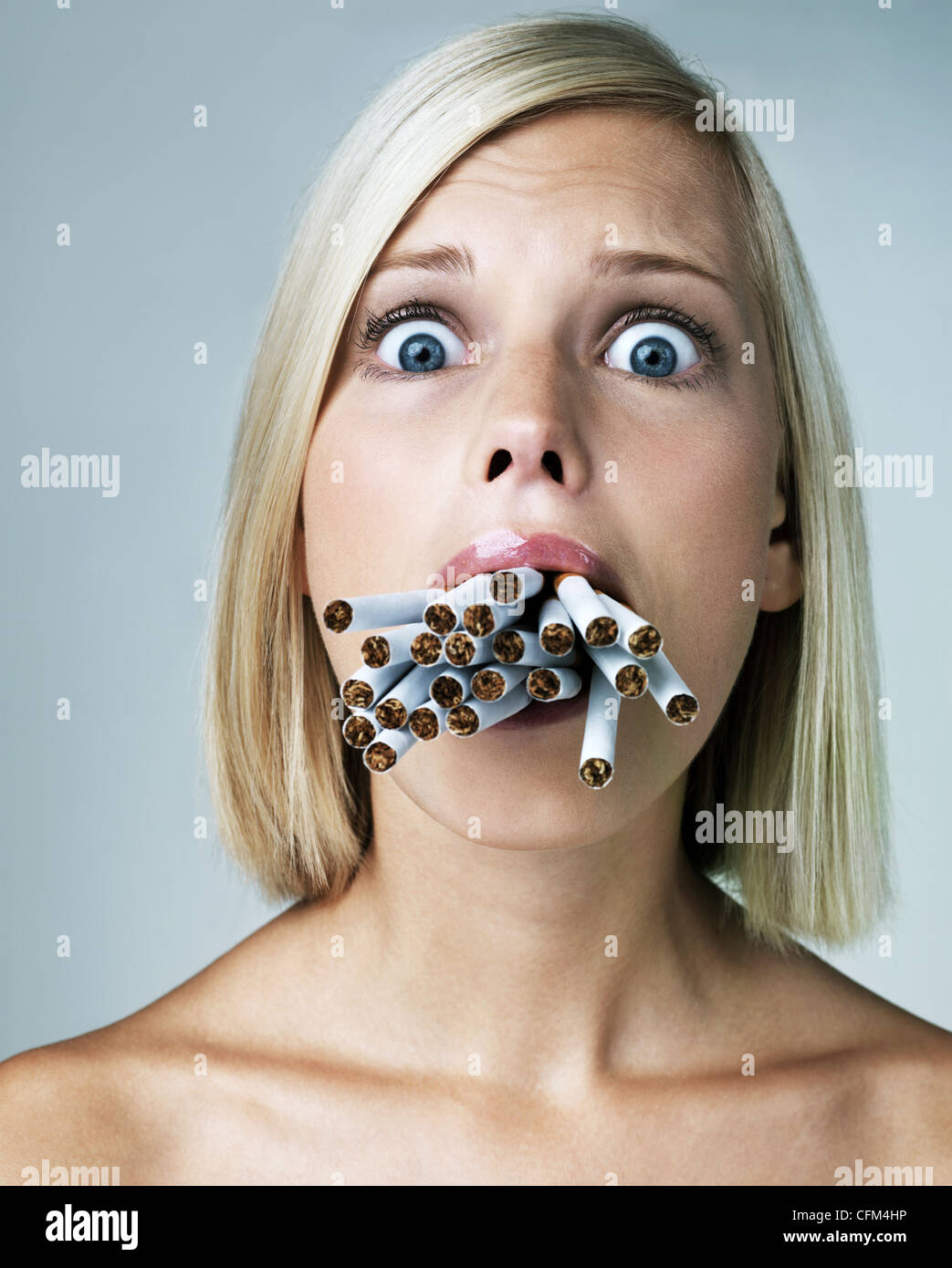Young woman looking alarmed with mouthful of cigarettes, studio shot ...
