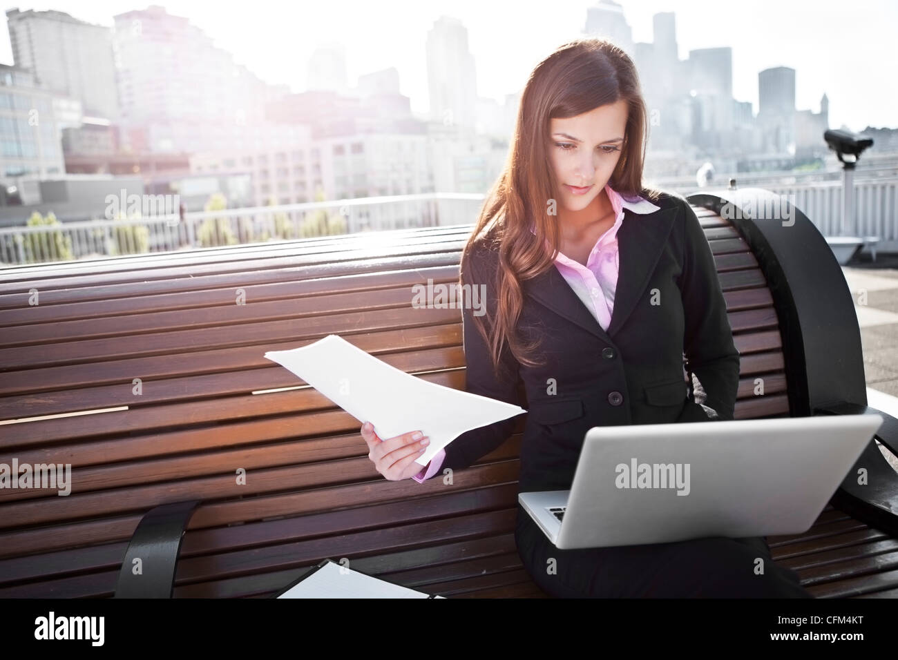 USA, Seattle, Young businesswoman sitting on bench and working Stock ...