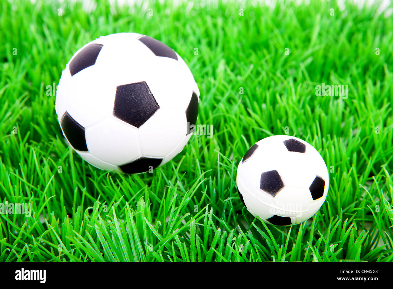 One big and one little soccer ball on plastic grass Stock Photo - Alamy