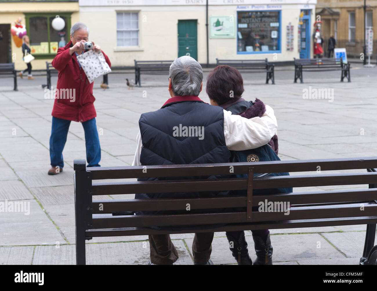 A Chinese man taking a photograph of two people embracing sitting on a ...