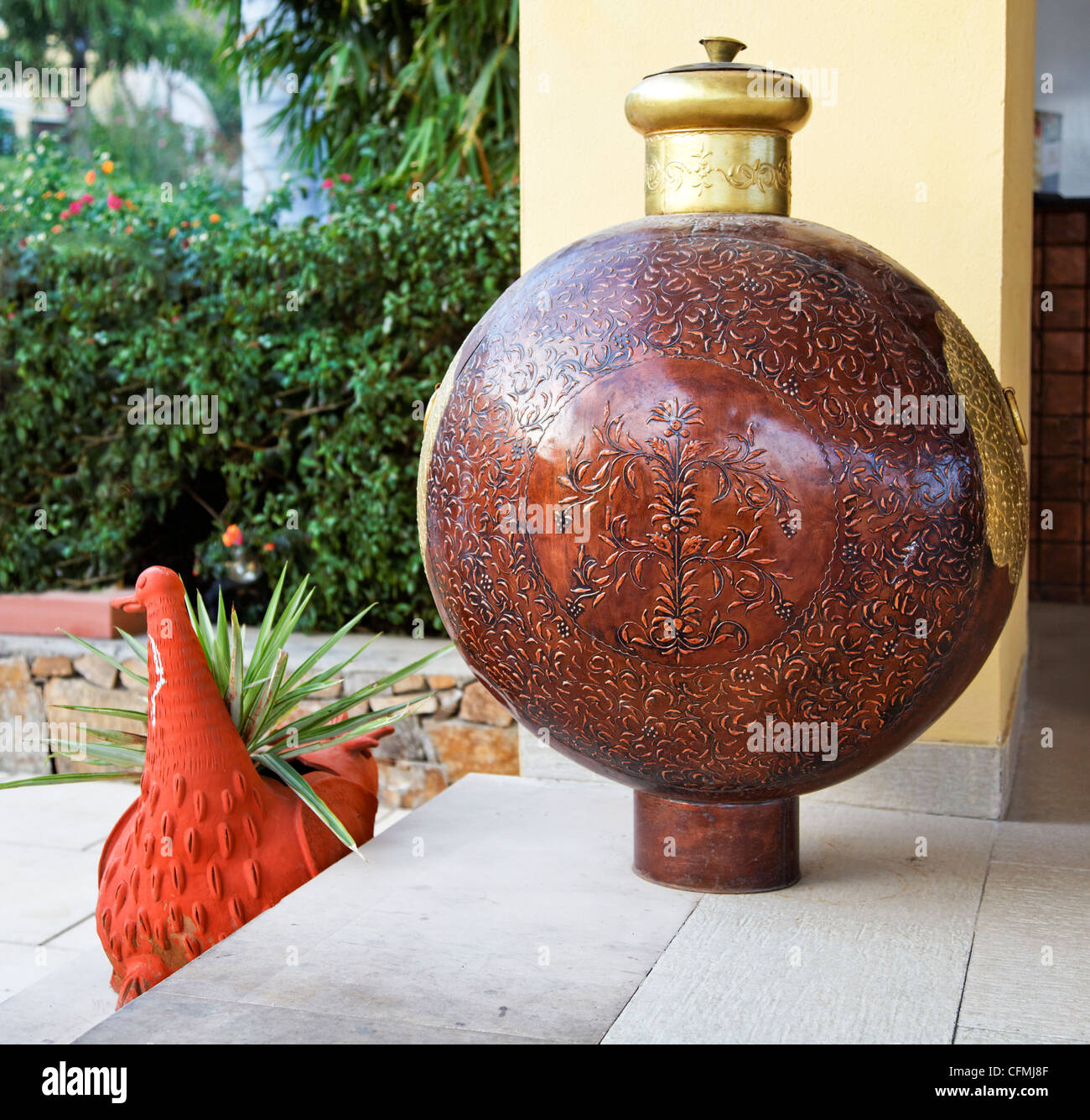 square format of ornately carved copper bottle used as a garden feature ...