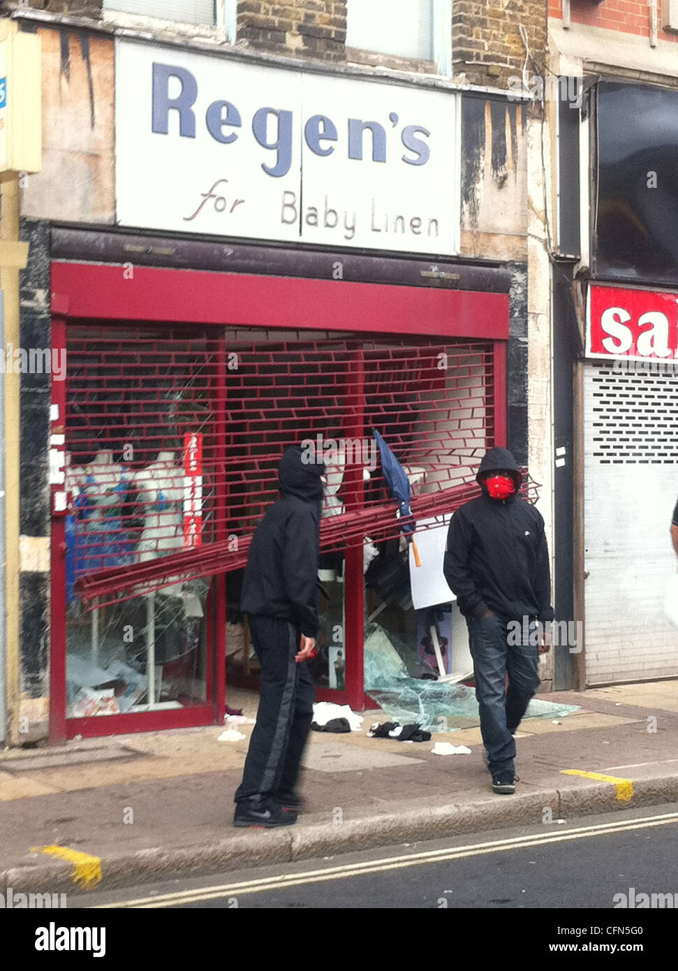 Youths wearing scarfs stand outside a looted clothes Shop in Peckham ...