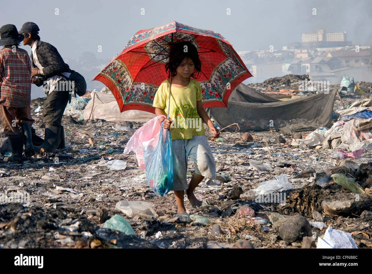 A young child laborer girl is carrying an umbrella to shade herself at ...