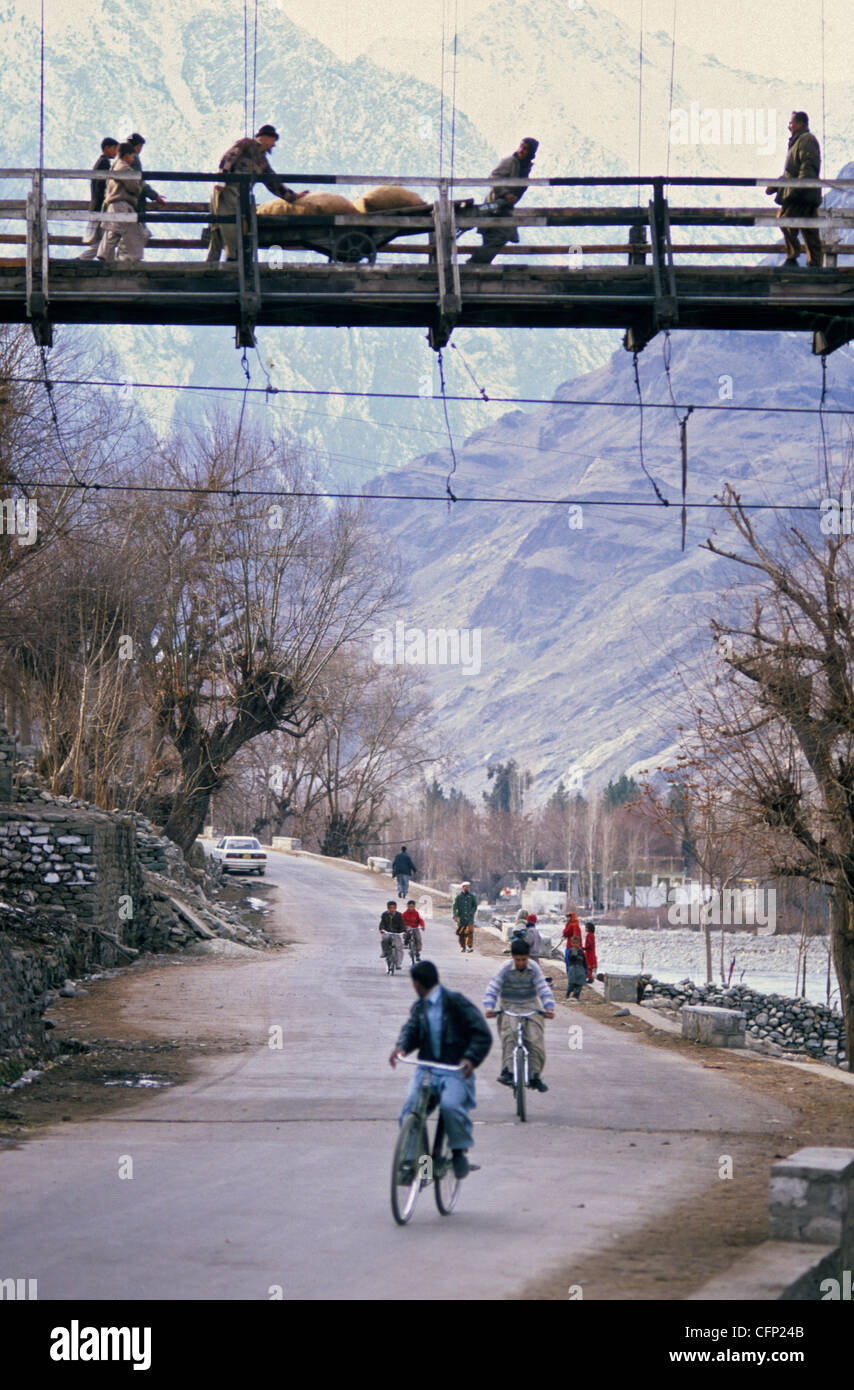 Scene on the streets of Gilgit with people crossing a suspension bridge ...