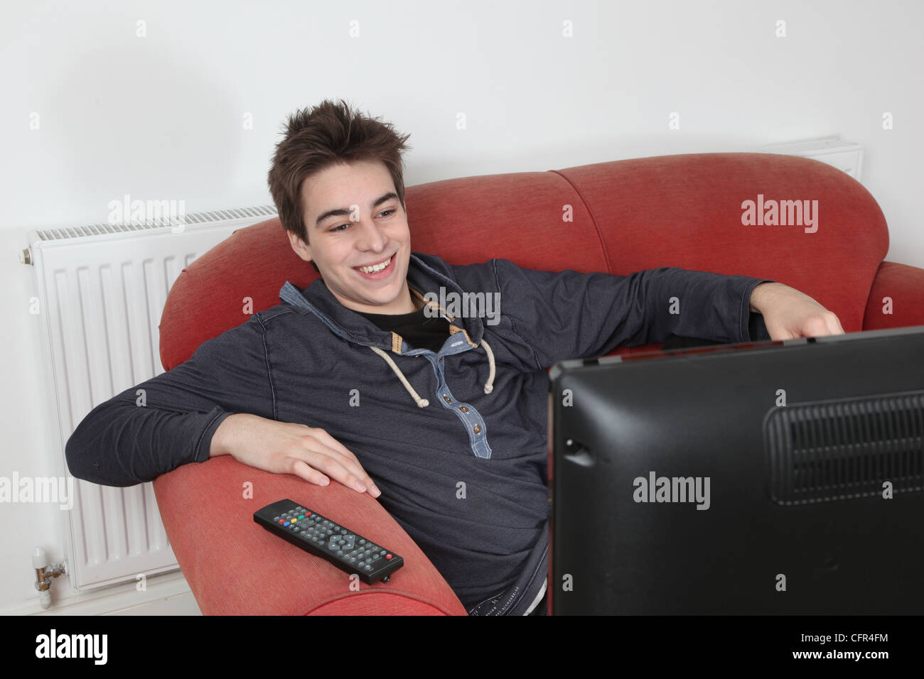 Young man smiling watching tv on his own Stock Photo - Alamy