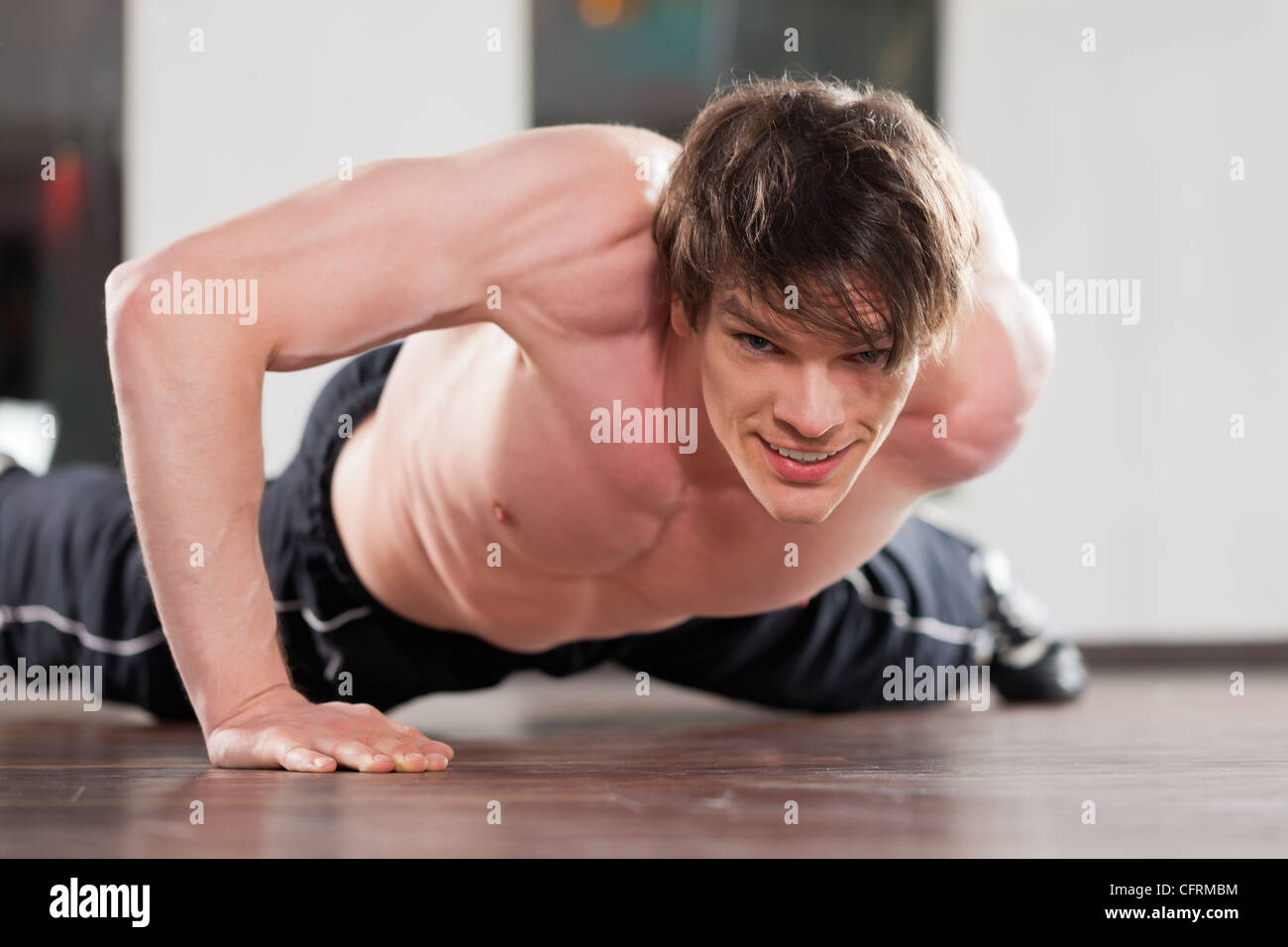 Muscular man exercising by doing pushups with only one arm in a gym ...