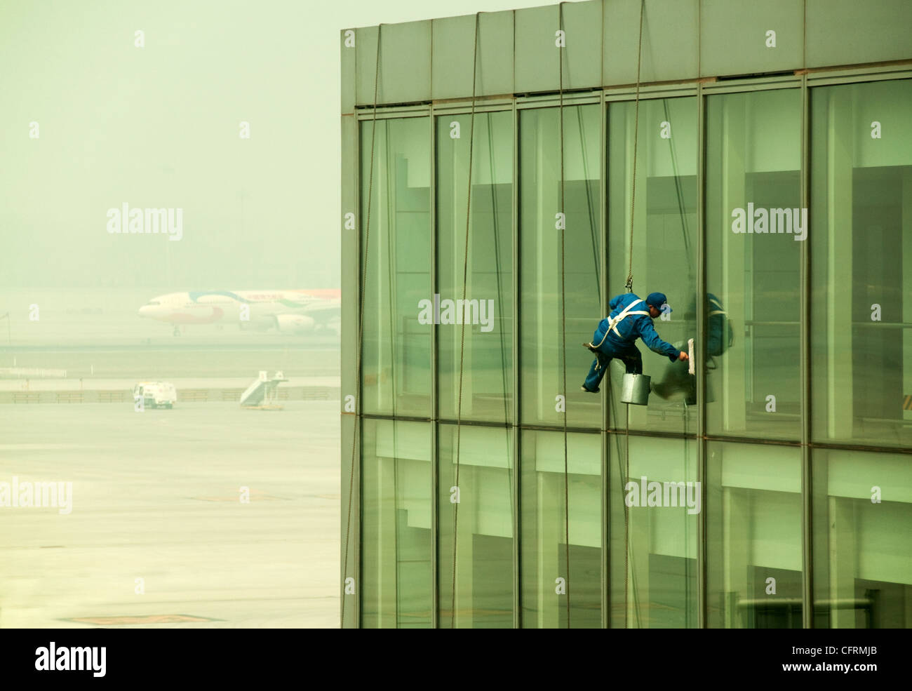 Hanging window cleaner at Beijing Airport with an aircraft on the ...