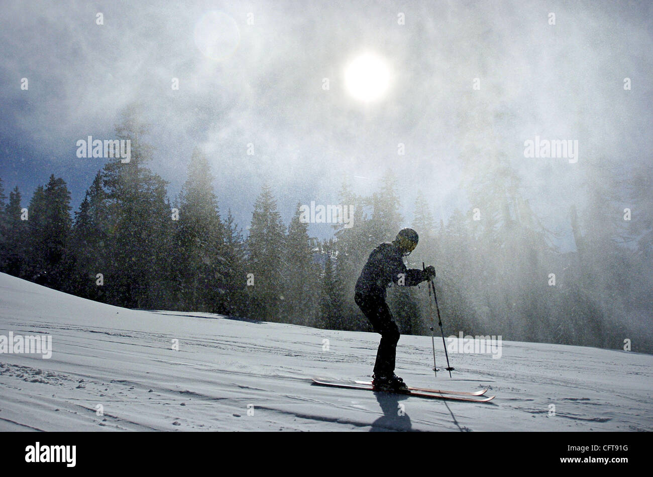 A skier heads down a hill under as a snow machine blows snow on a sunny ...