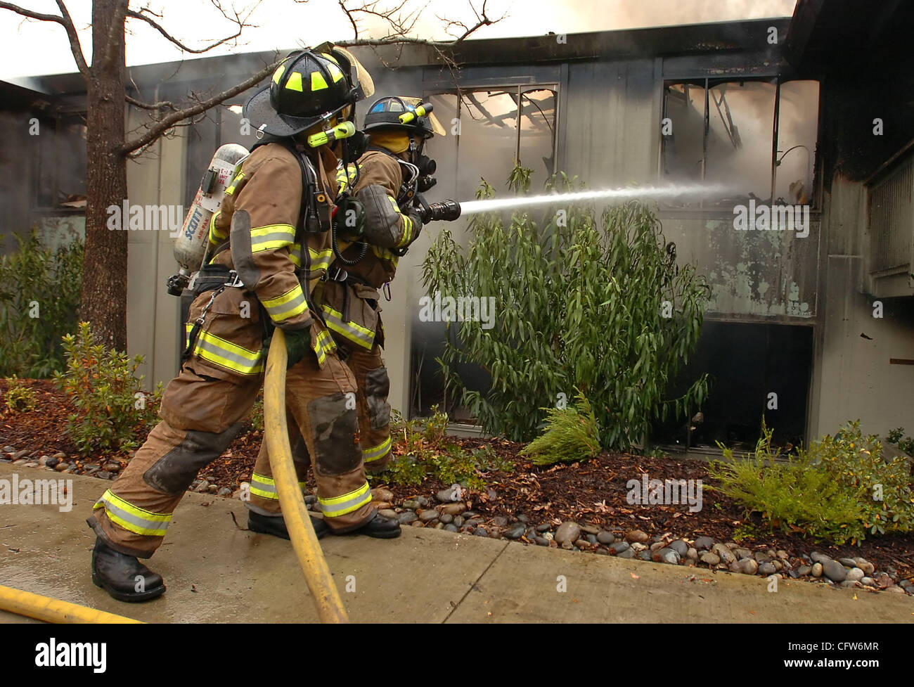 Firefighters spray water on a second level of a three-alarm structure ...