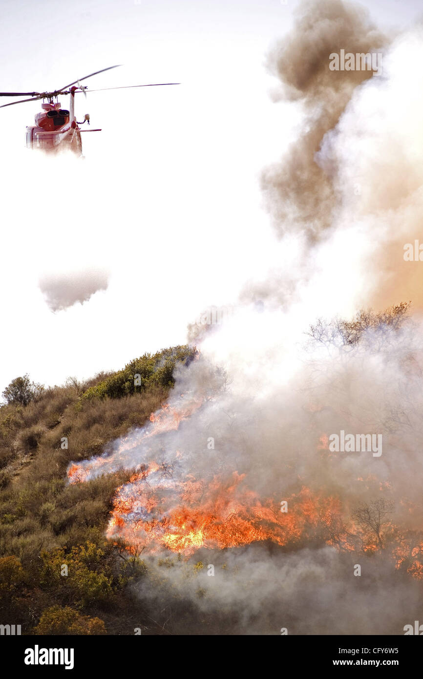 A water dropping chopper douses a brush fire, burning out of control in ...
