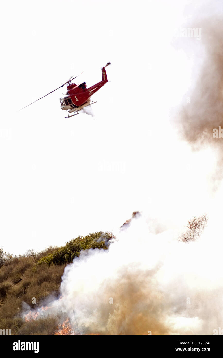 A water dropping chopper douses a brush fire, burning out of control in ...