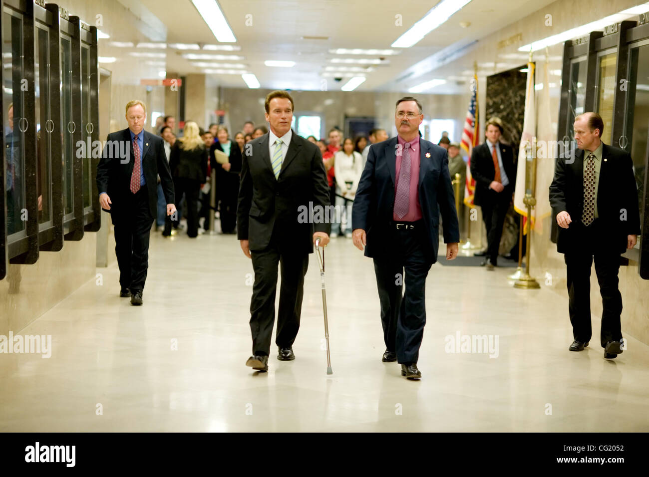Using a cane, Governor Arnold Schwarzenegger walks with Jim Tilton ...