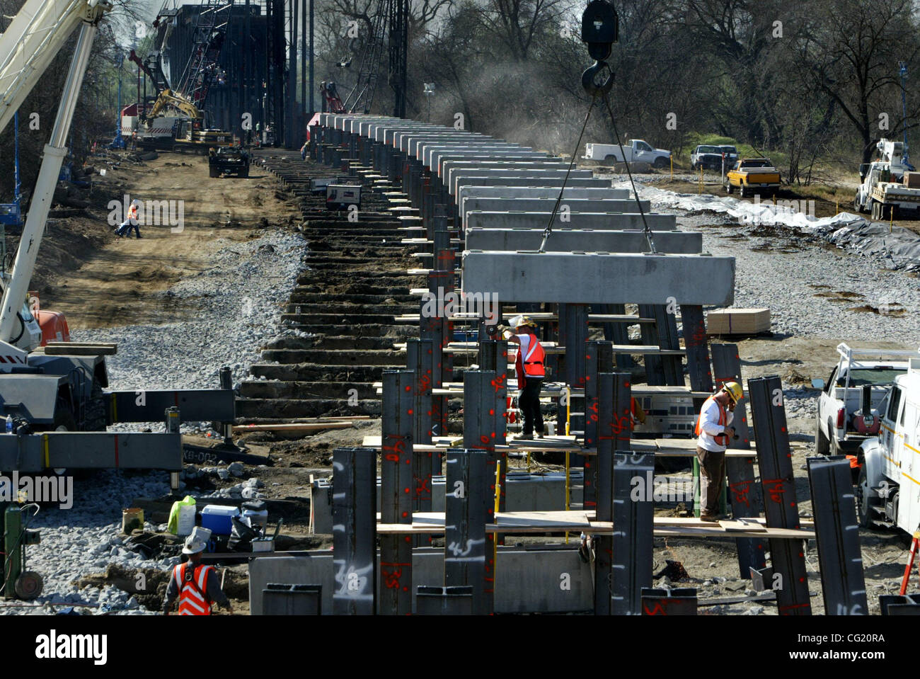 A crane lowers a support beam for the railroad track as workers cut and ...