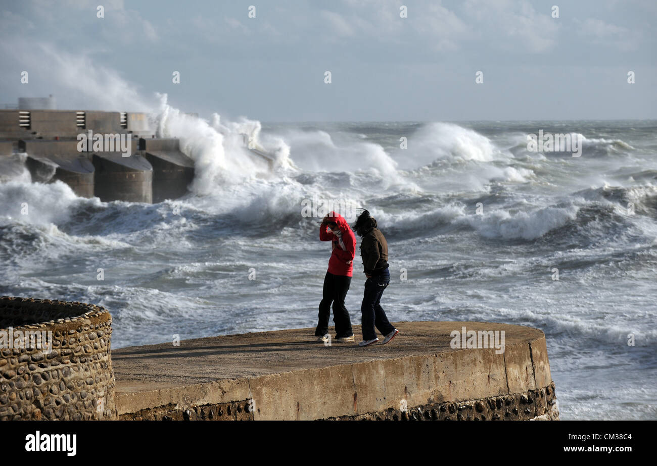 Standing against the wind two people watch massive waves crash over ...