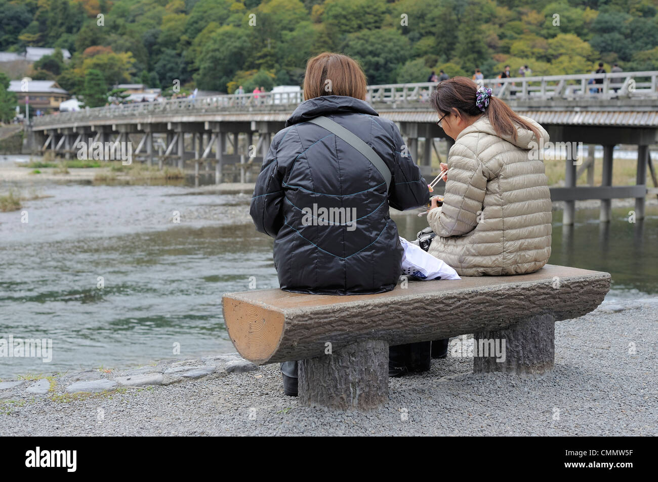 two Japanese women eating sushi in front of the Togetsu-kyo bridge in ...