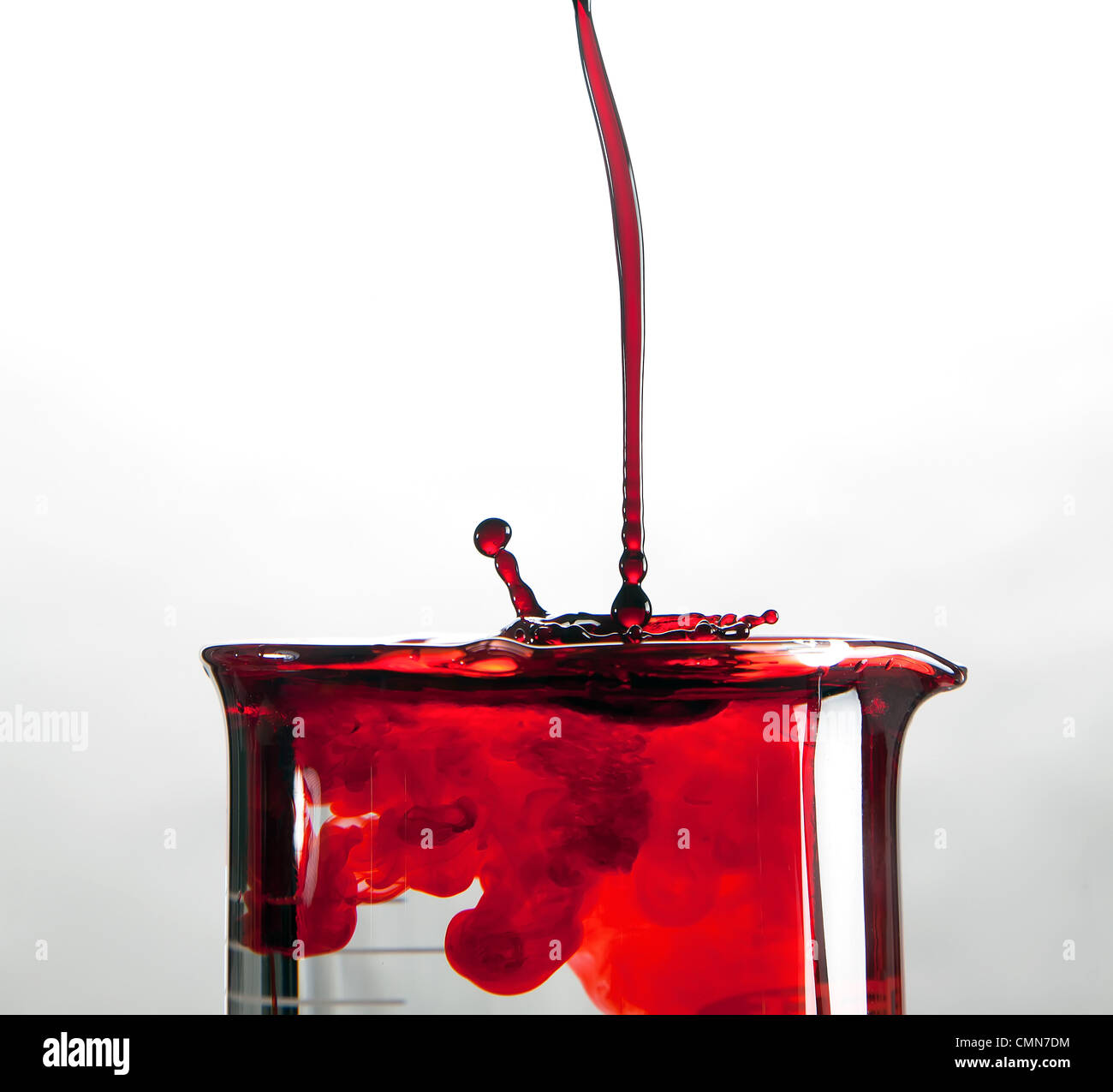 A close up of a glass medical beaker with red colored fluids pouring in ...
