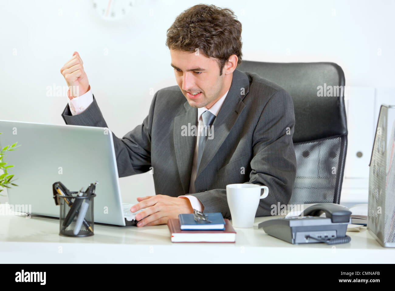 Angry modern businessman sitting at office desk and menacingly ...